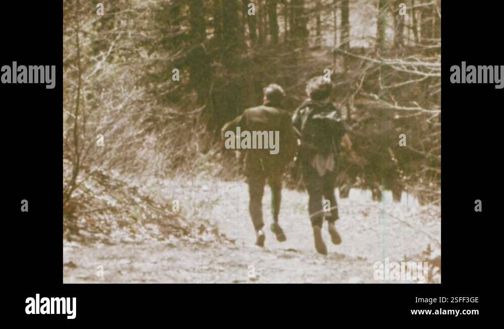 1970s: Two boys run through the woods with a rifle. One boy points. A ...