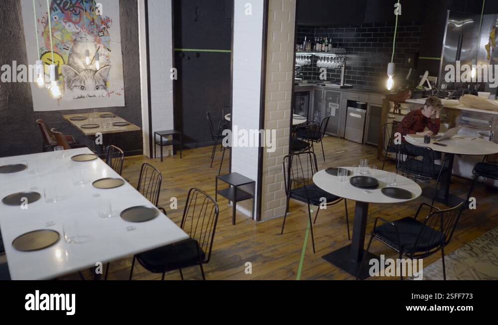 Pan of interior of modern restaurant where owner sits alone at table ...
