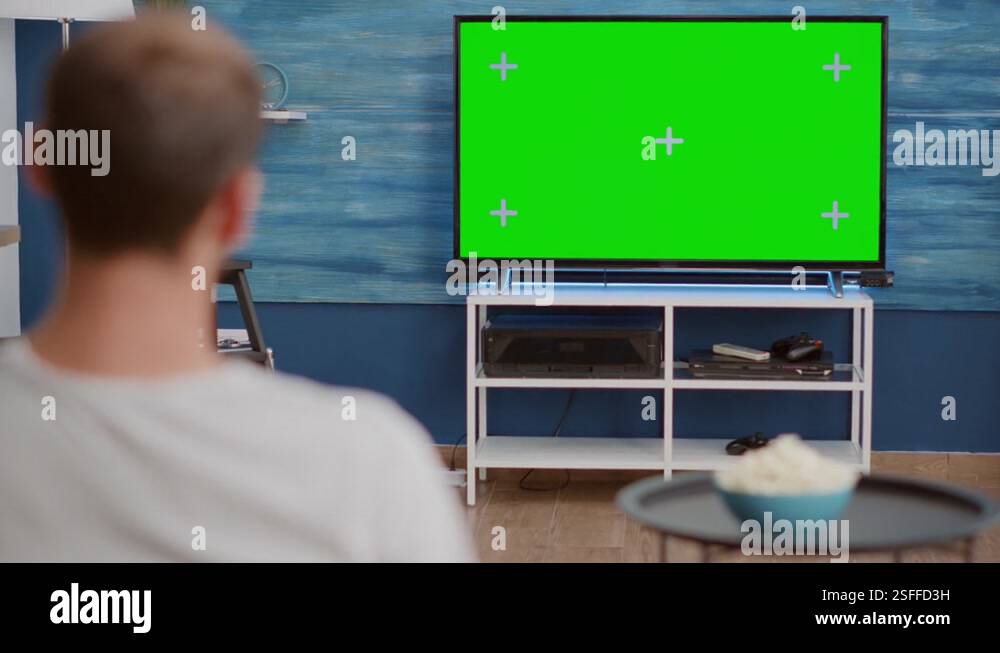 Over shoulder view of man switching channels while looking at green ...