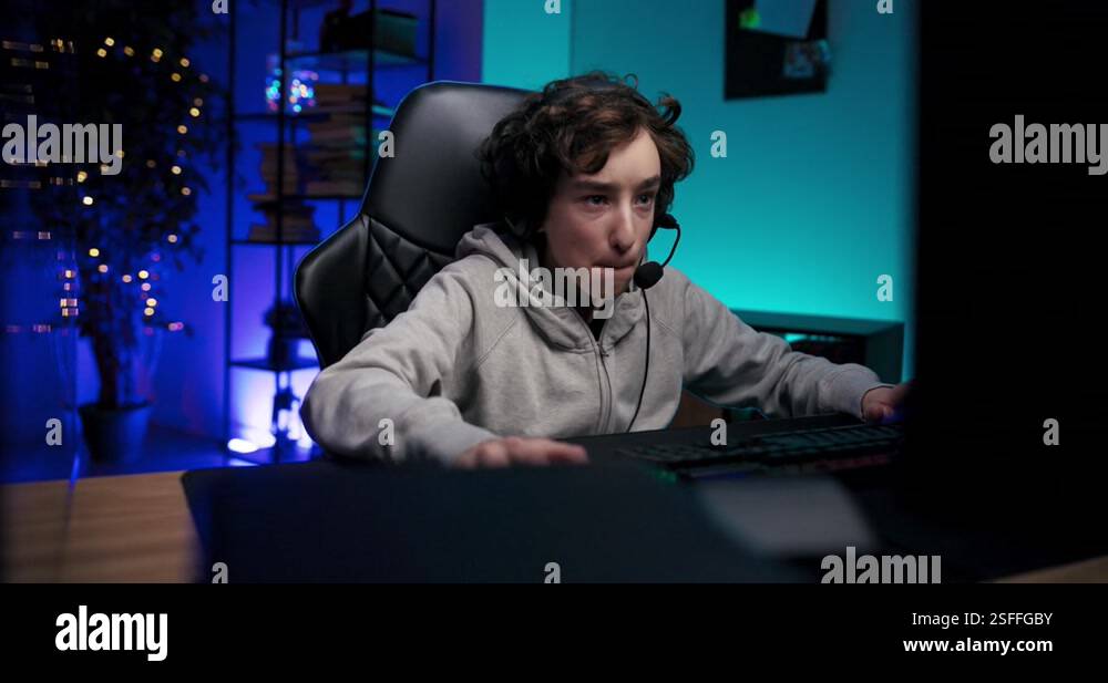Small gamer with headset, boy sits in front of computer monitor late at ...