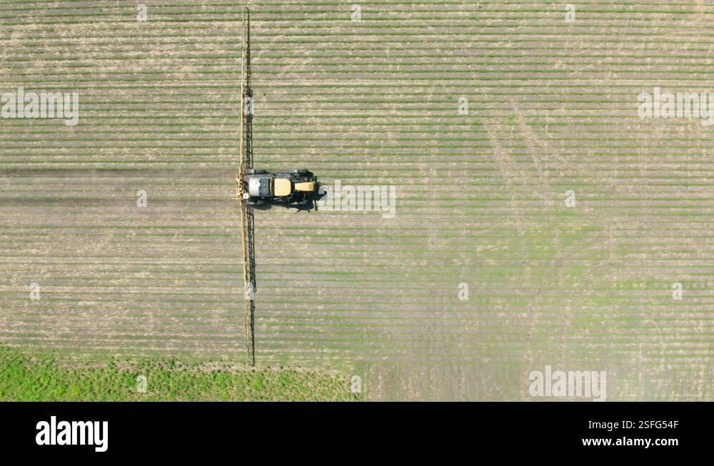 Aerial top down, farm tractor spraying crops with pesticide and ...