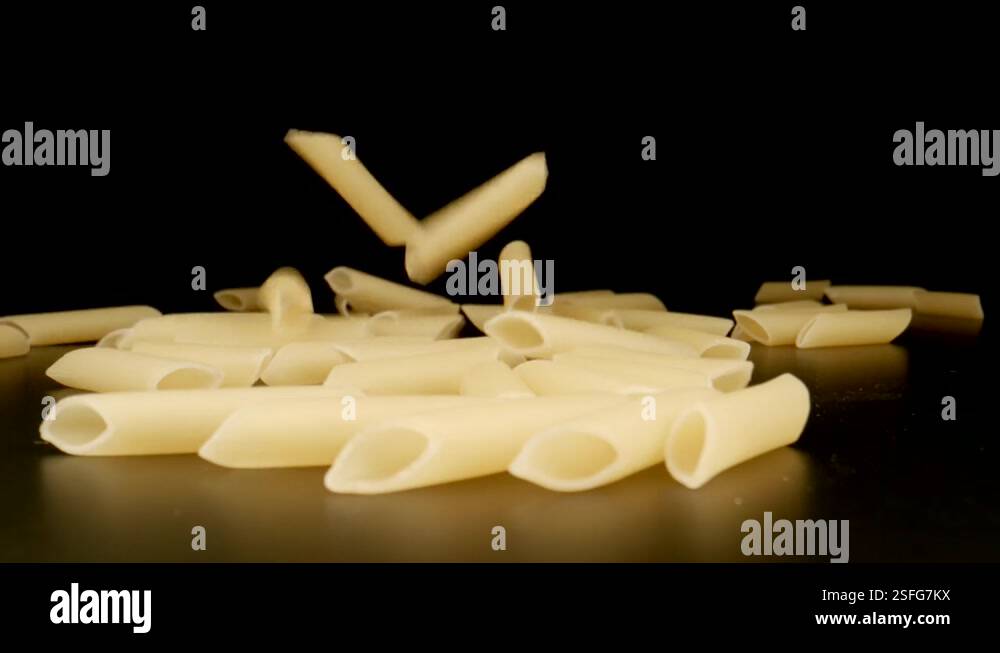 MACRO: Uncooked penne rigate pasta fall on a black table, Slow motion ...