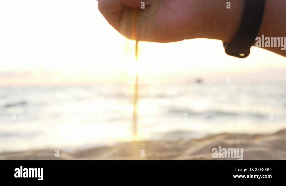 White sand pours through the fingers of a man's hand. male hands hold ...