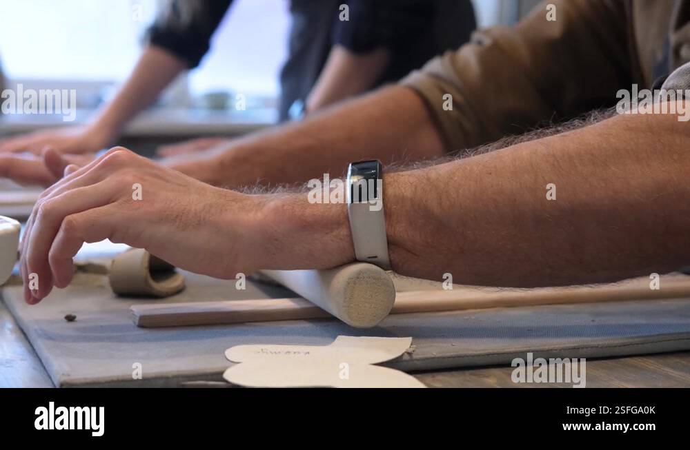 A close-up of a male and female hands potter rolls a clay rolling pin ...