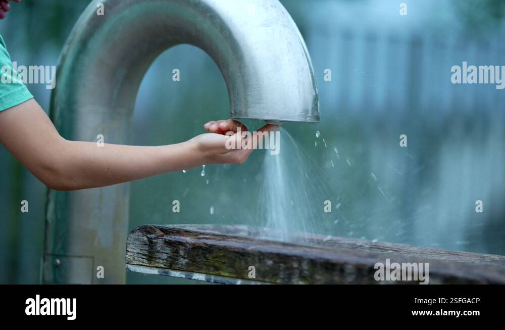 Child playing with public water faucet pressing finger splashing water ...