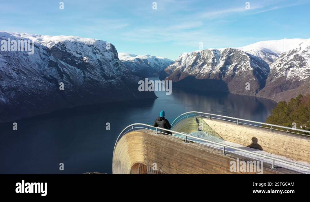 Flying slowly above man relaxing on edge of spectacular Stegastein ...