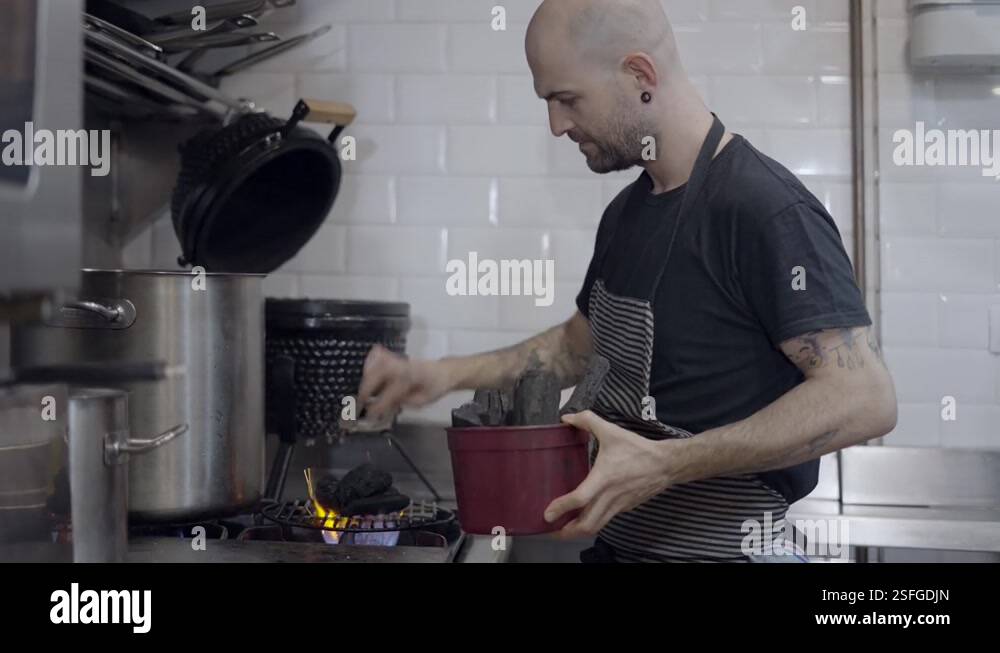 Chef puts charcoal on grill grate in restaurant kitchen, side view ...