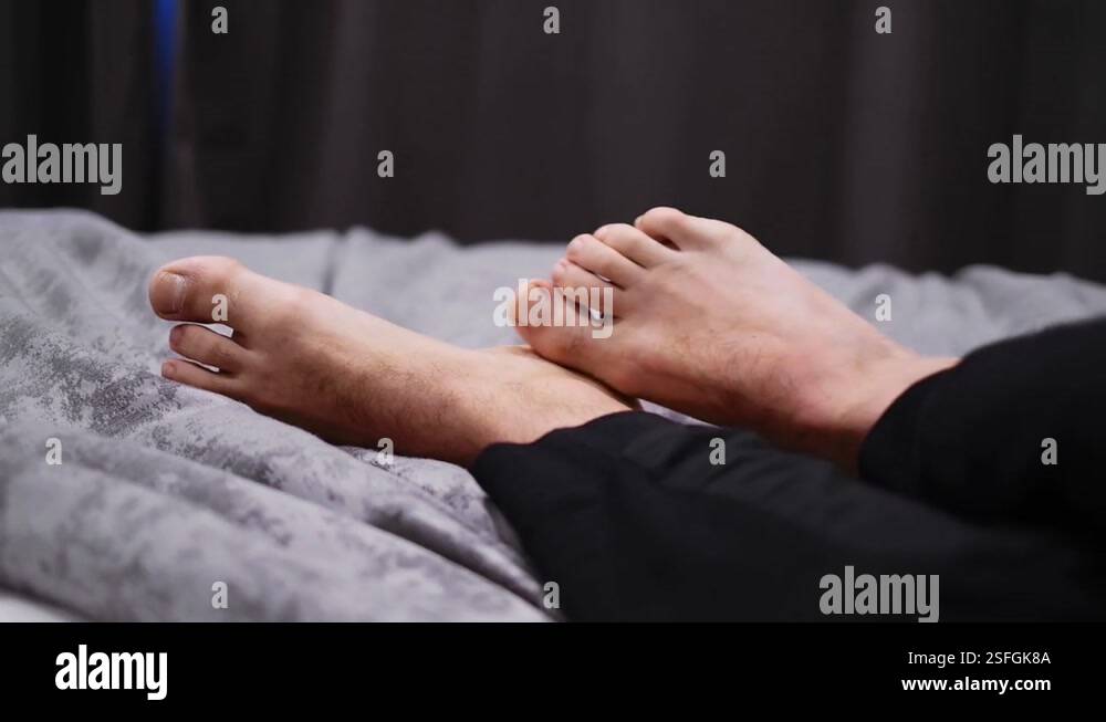 Close-up of male legs with feet forward lying on the bed while resting ...