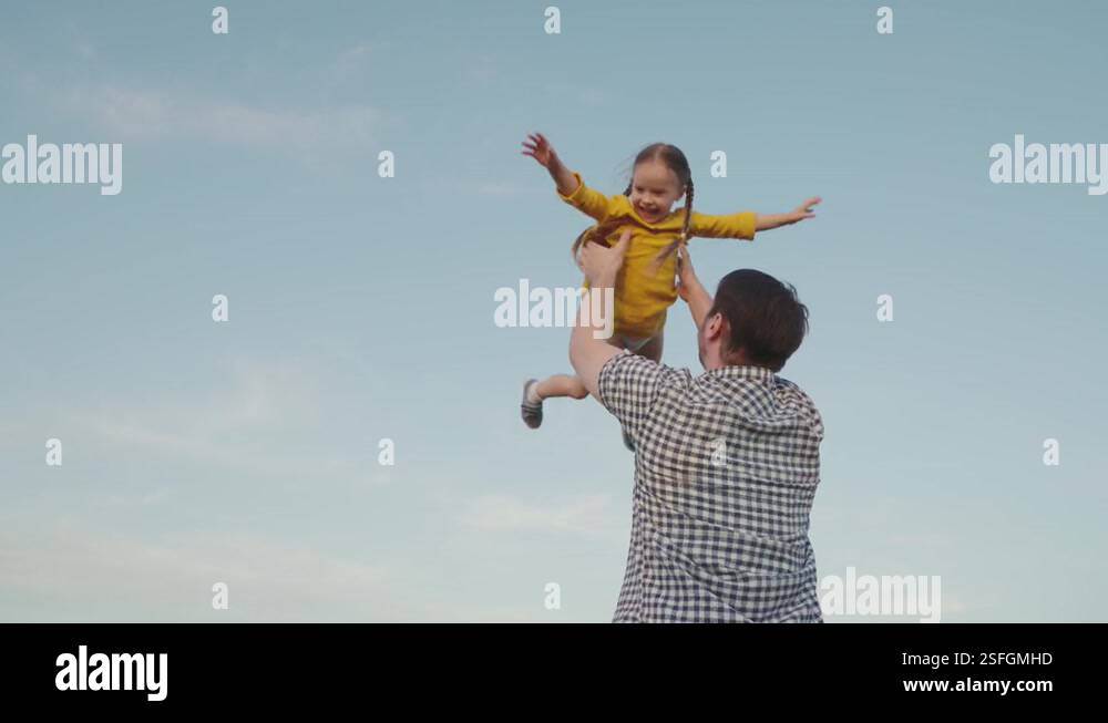 father throws little cheerful child into blue sky. kid laughs with his ...