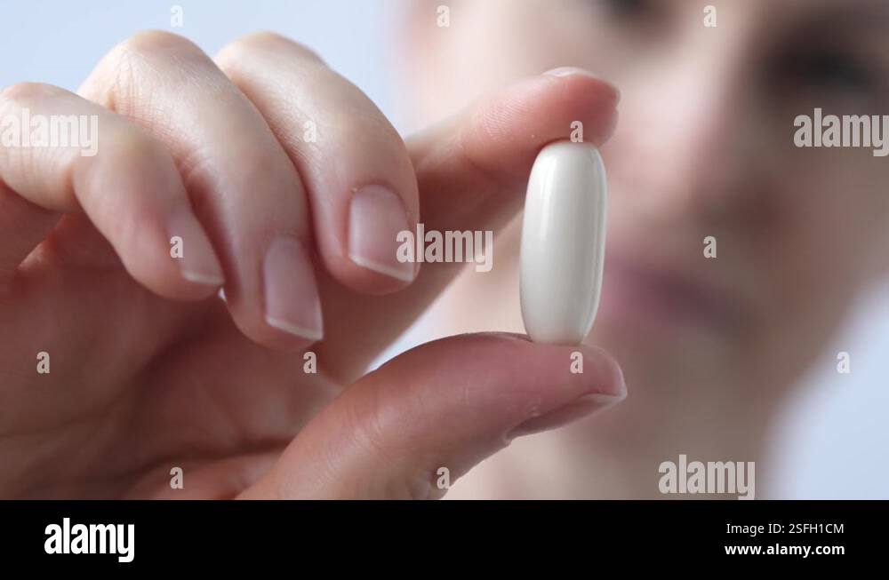 A woman holds a large white pill in her hand and examines it carefully ...