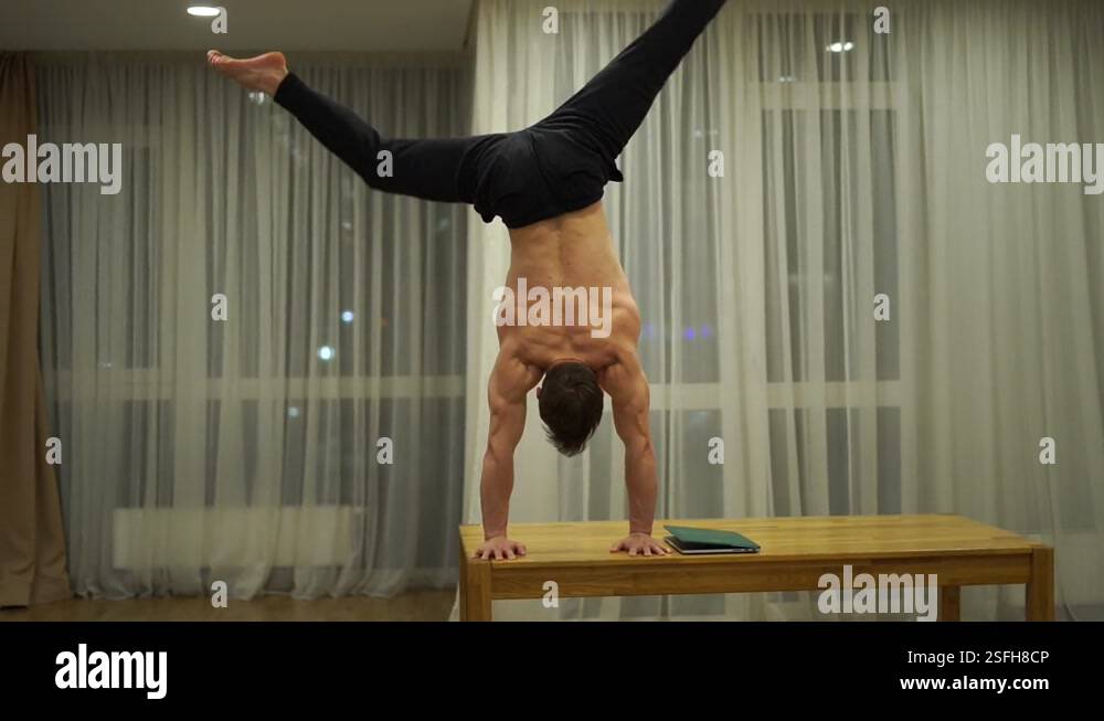 A muscular man keeps balance on one hand and uses laptop. Self ...