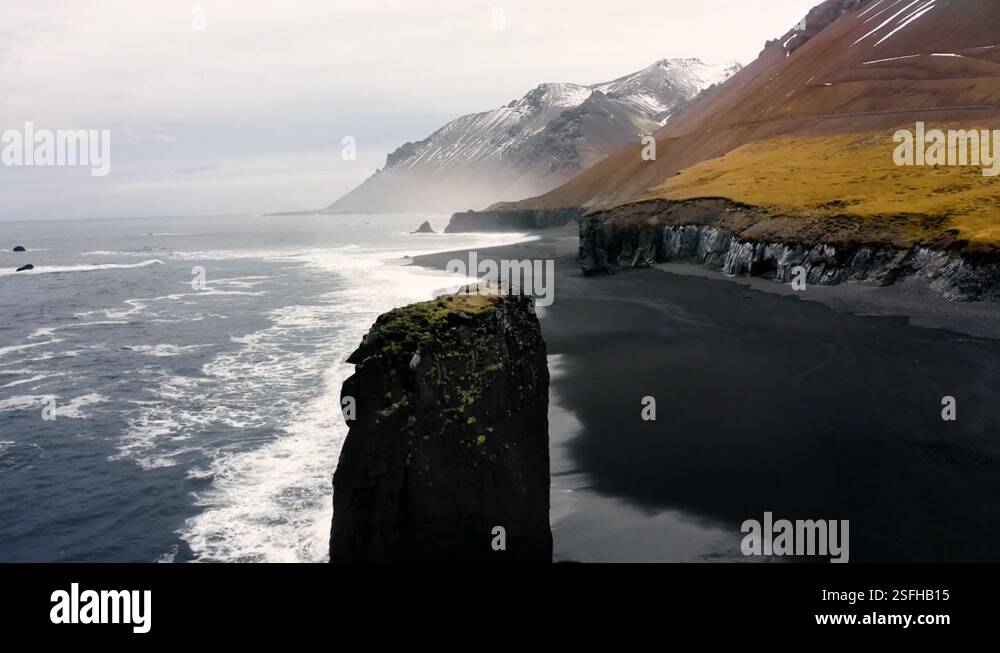 Alone Cliff washed by ocean waves on a black beach in Iceland ...