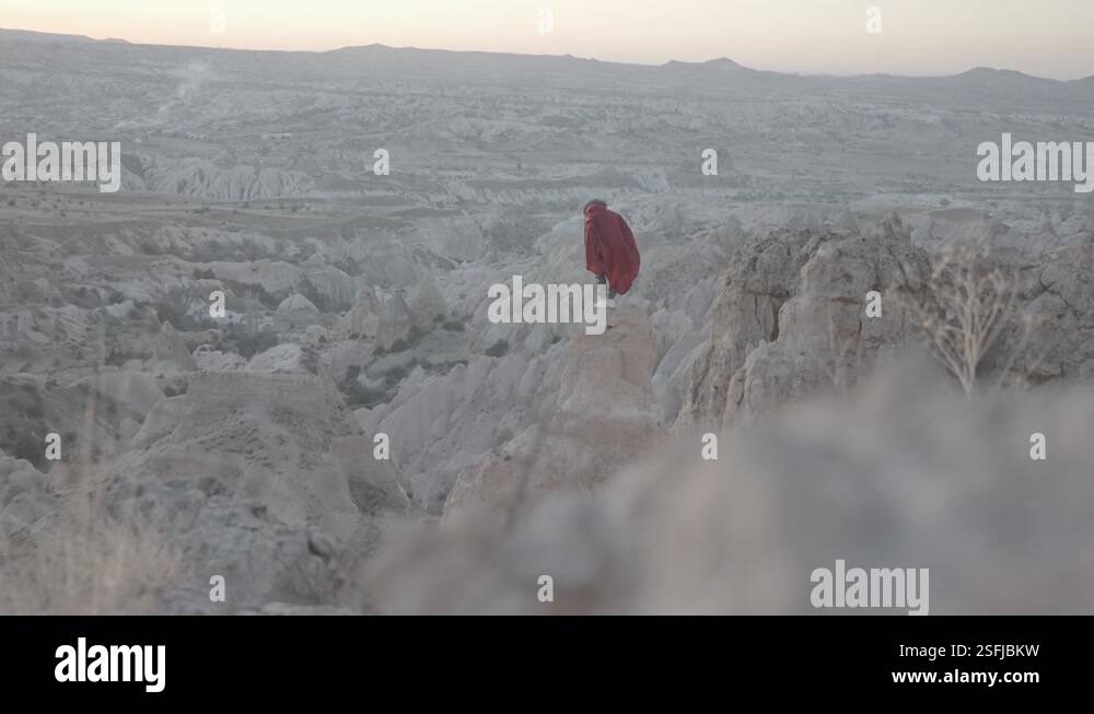 Person in a red blanket standing on a thin spire and cliff during ...