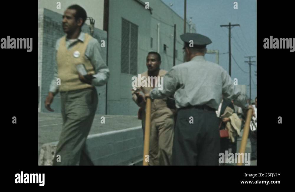 1960s: Person holds up film slate. Line of people walk past guard. Man ...