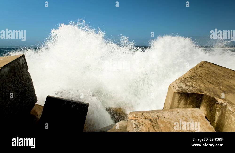 Incessant waves crash into dolosse protecting the harbour wall ...