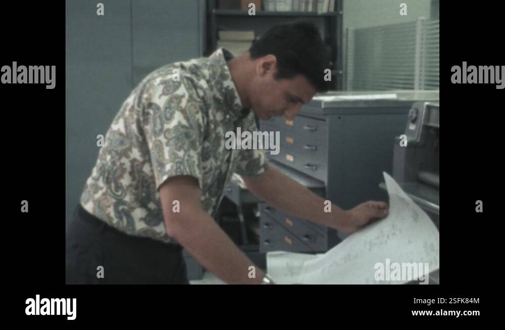 1960s: Man leans over table, looks at paper. Man shakes another person ...