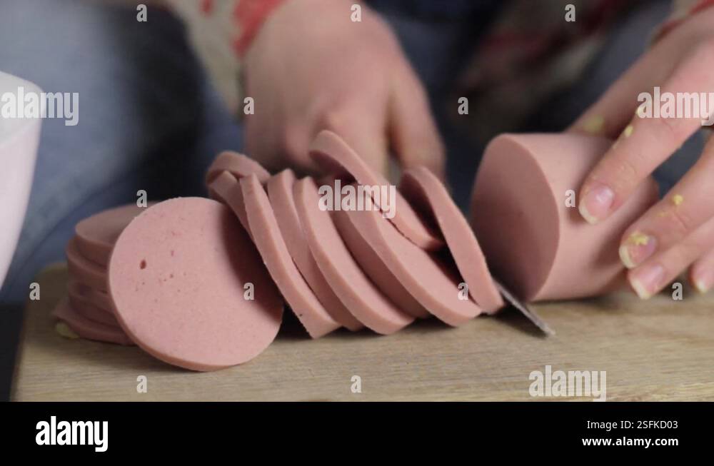 Person slices doctor's sausage with sharp knife of wooden board, close ...