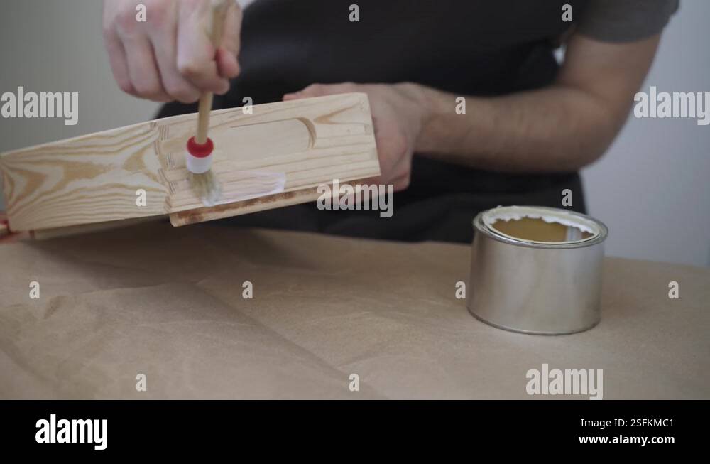Master paints varnish to side of wooden box with round brush, close-up ...