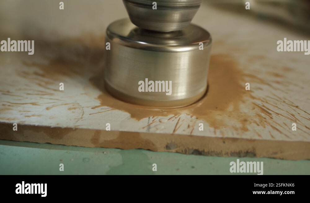 worker drills a round hole in ceramic tile with diamond crown, closeup ...