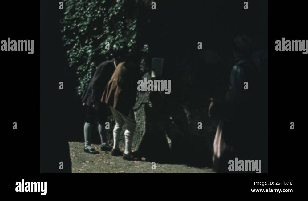 1800s: men in 1800s breeches stoop to read poster on French wall. Lady ...