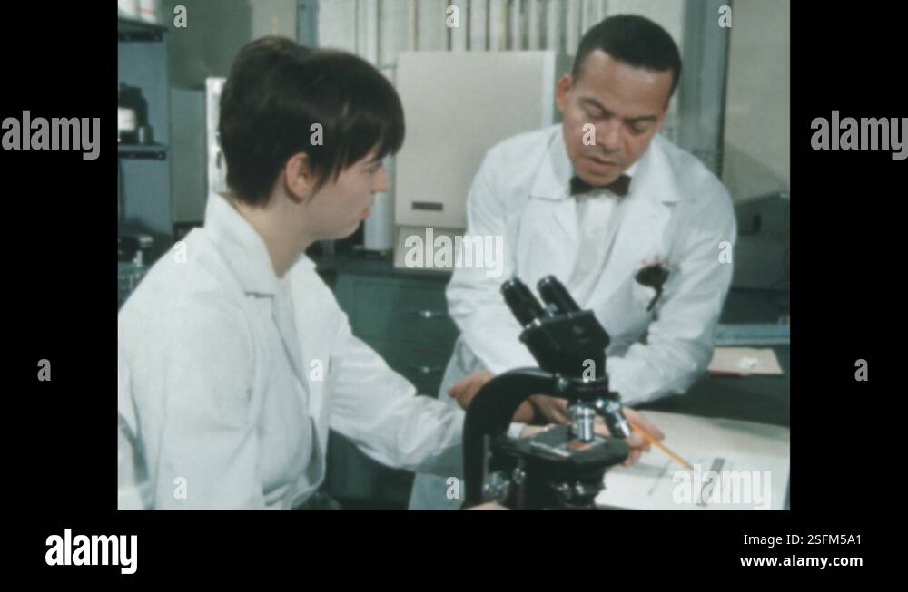 1960s: Lab. Test tubes. Man and woman speak. Woman looks in microscope ...