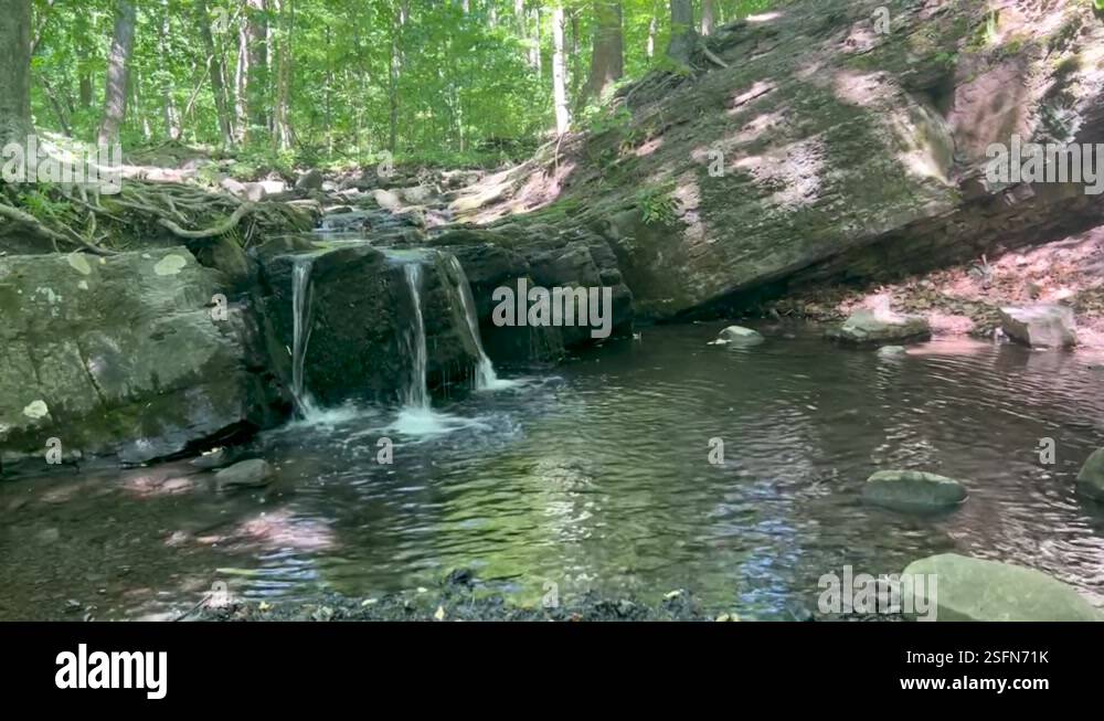 Idyllic waterfall flows over rock formations with strata in lush ...