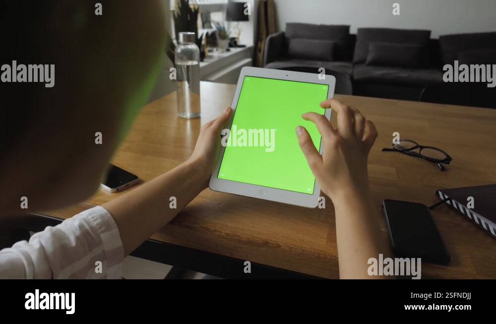 Person using tablet with green screen at home while sitting near table ...
