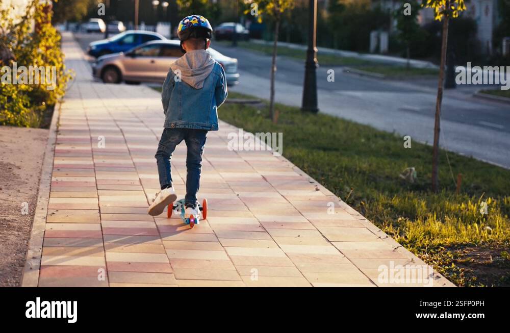 Cute boy learning to ride kick scooter on a street. Child wearing ...