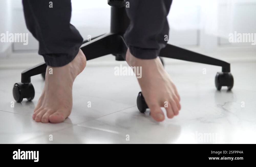 Barefoot men's feet on an office chair with wheels on white porcelain ...