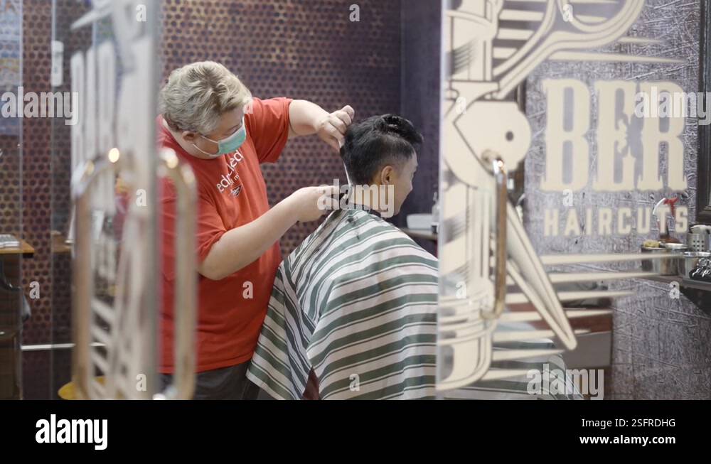 A side view of a happy guy getting haircut by hairdresser in a salon ...