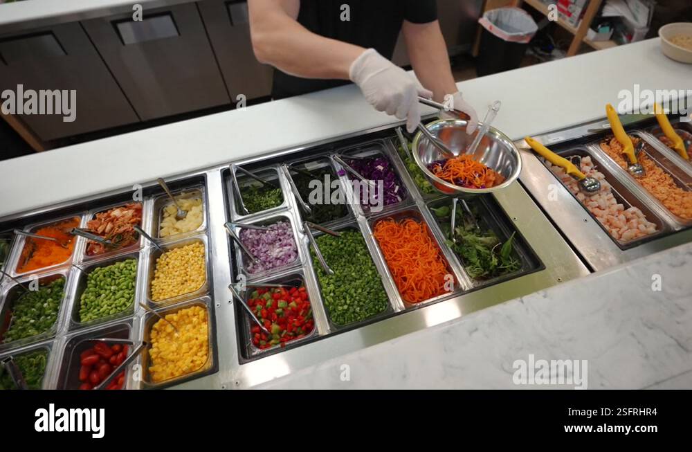 Employee builds a colorful salad at vegetable station in restaurant ...