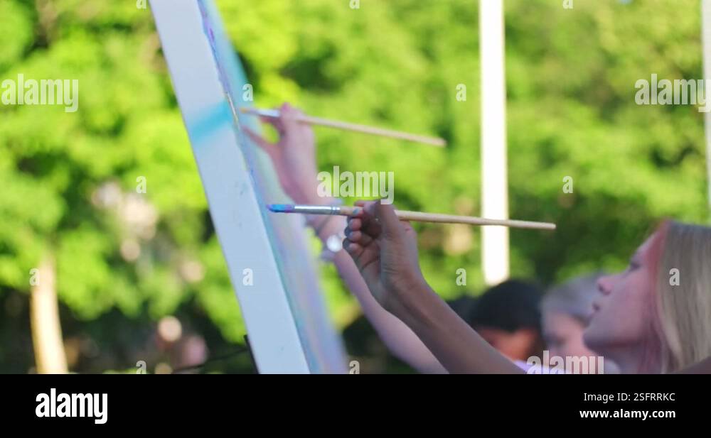 Side view shot a multiple people painting a big white canvas in a ...