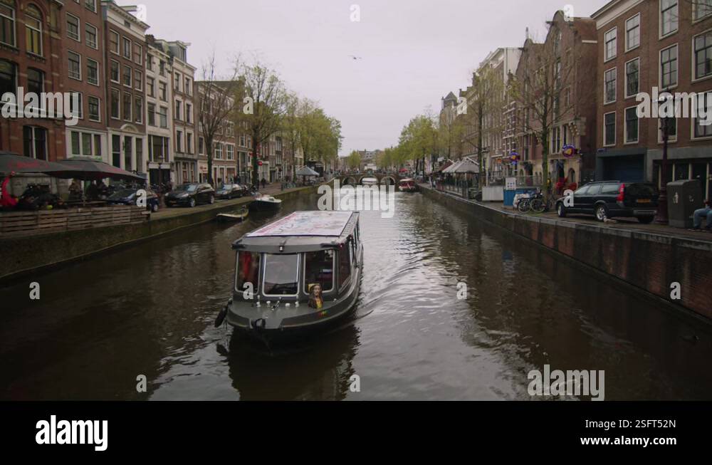 Smoke Boat cruising in old town Amsterdam canal on cloudy day, static ...