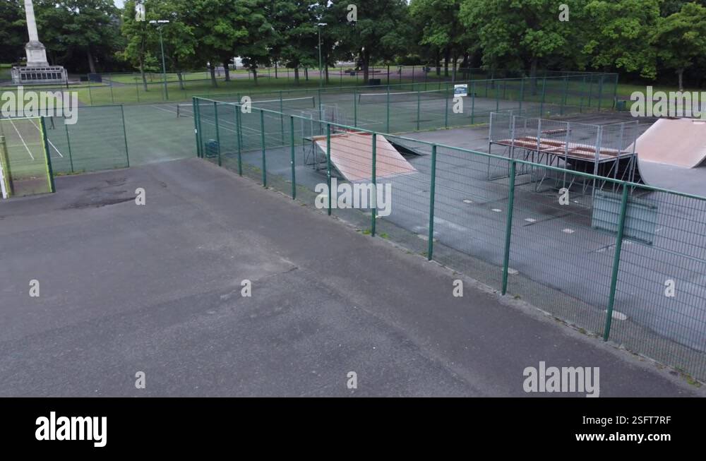 Aerial view flying low across fenced basketball court skate park ramp ...