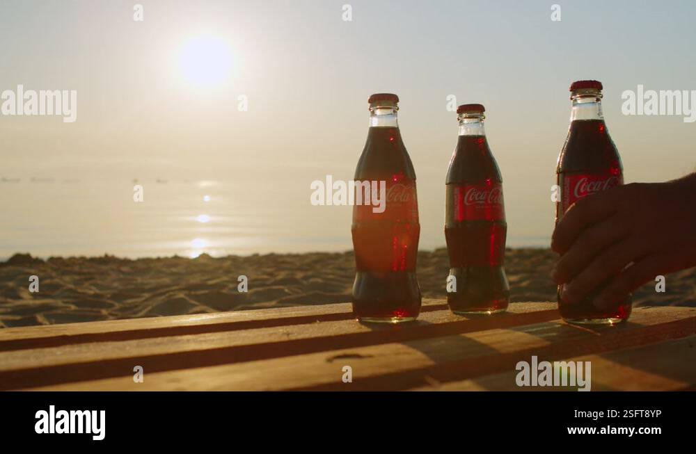 Three bottles Coca Cola sandy beach at sunrise. man hand takes bottle ...