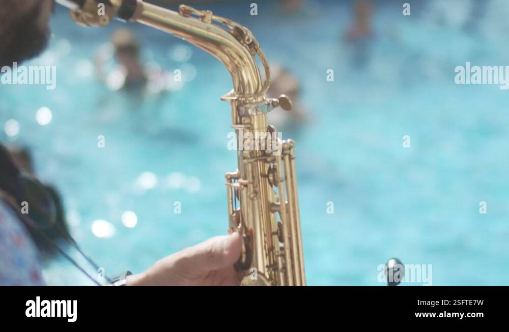 Male saxophonist plays the saxophone near the pool in the summer in a ...
