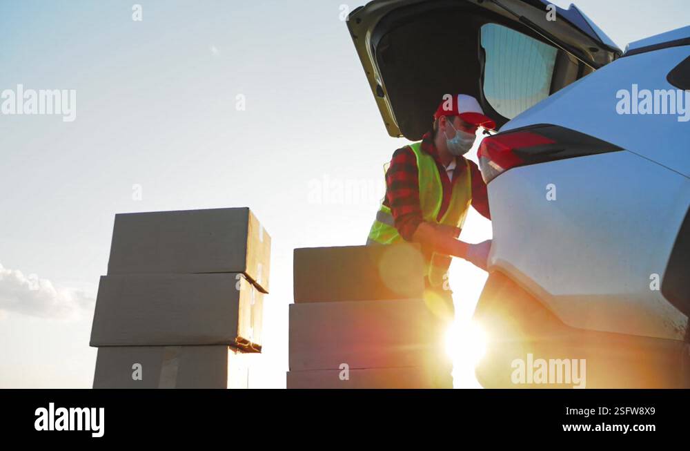 Delivery man in field in overalls loads sealed boxes with product ...
