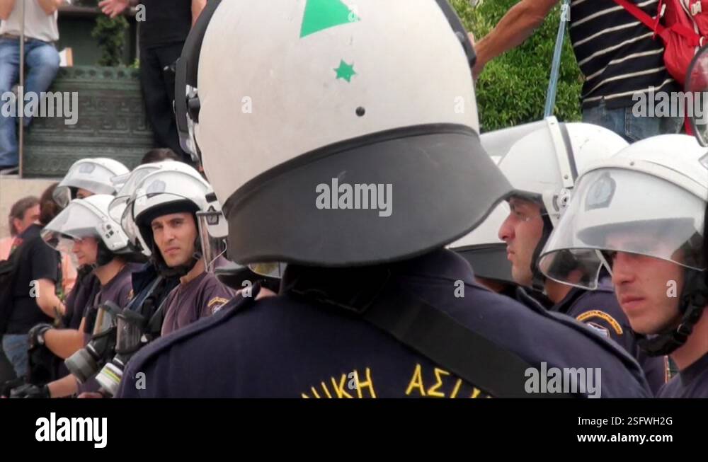 Greek riot police wearing helmets and gas masks stand in a line and ...