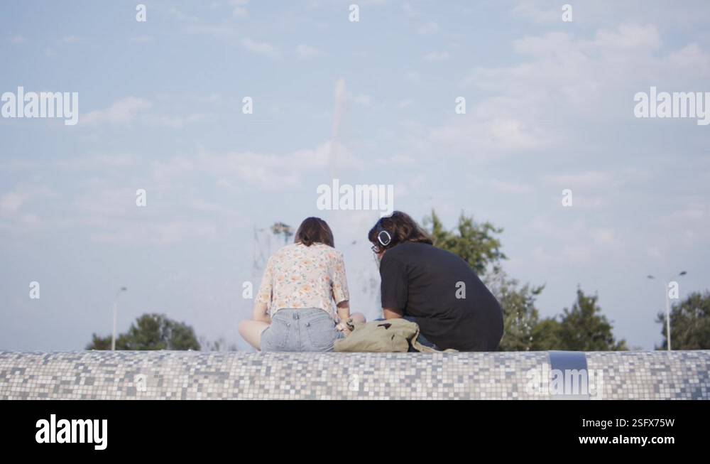 Back view of Two girls sit on outdoor and talk to each other. Sunset ...