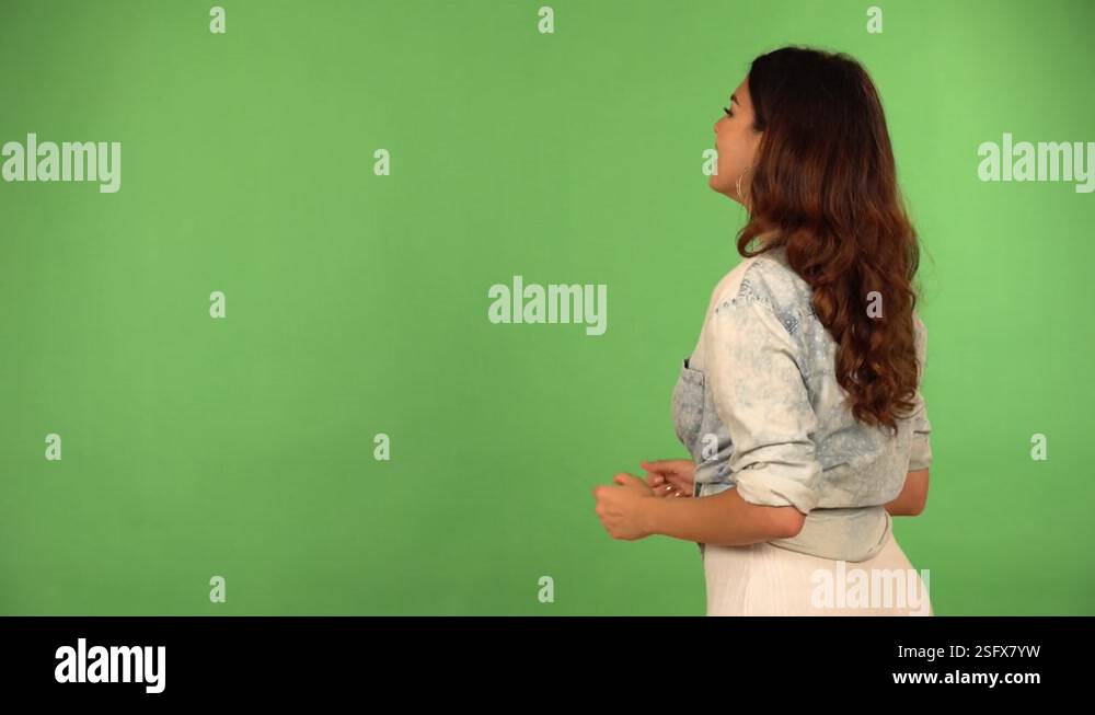 A young beautiful Caucasian woman cheers as she faces the green screen ...