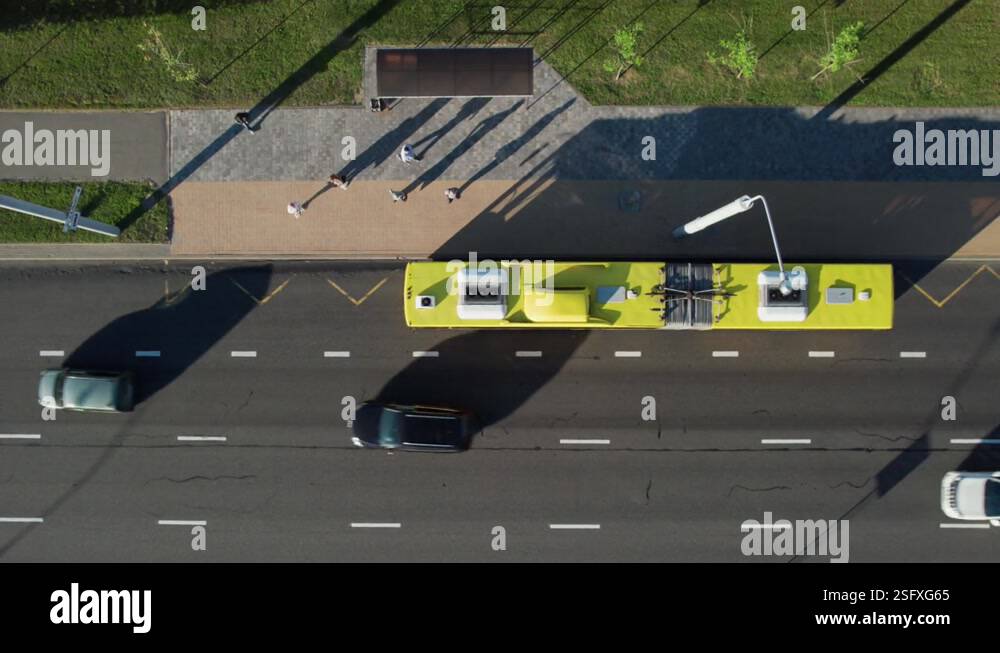 Aerial top view of a yellow city bus pulling up to the bus stop and ...