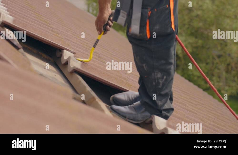 Closeup of worker using crowbar to remove roof tiles for solar panel ...
