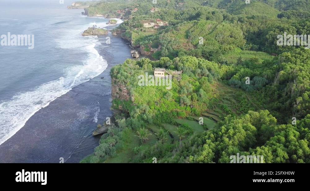 a building on the top of cliff border with the sea. drone shot of beach ...