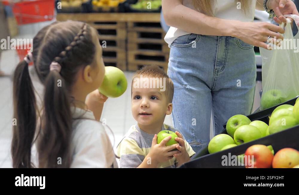 A mother with her daughter and son collects green apples in a bag in ...