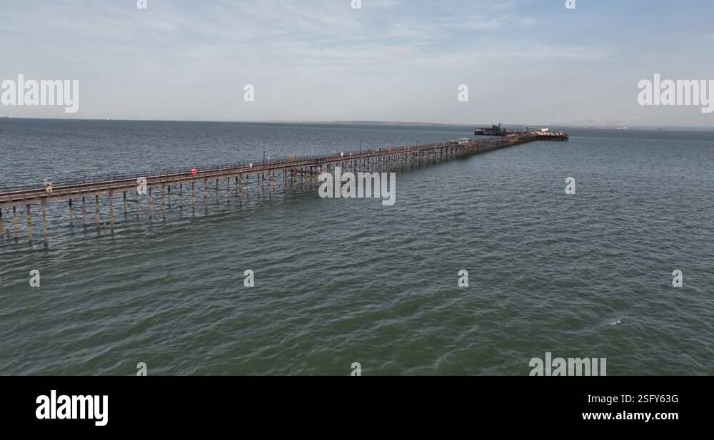 Long pier far in Thames river estuary, train driving on tracks above ...