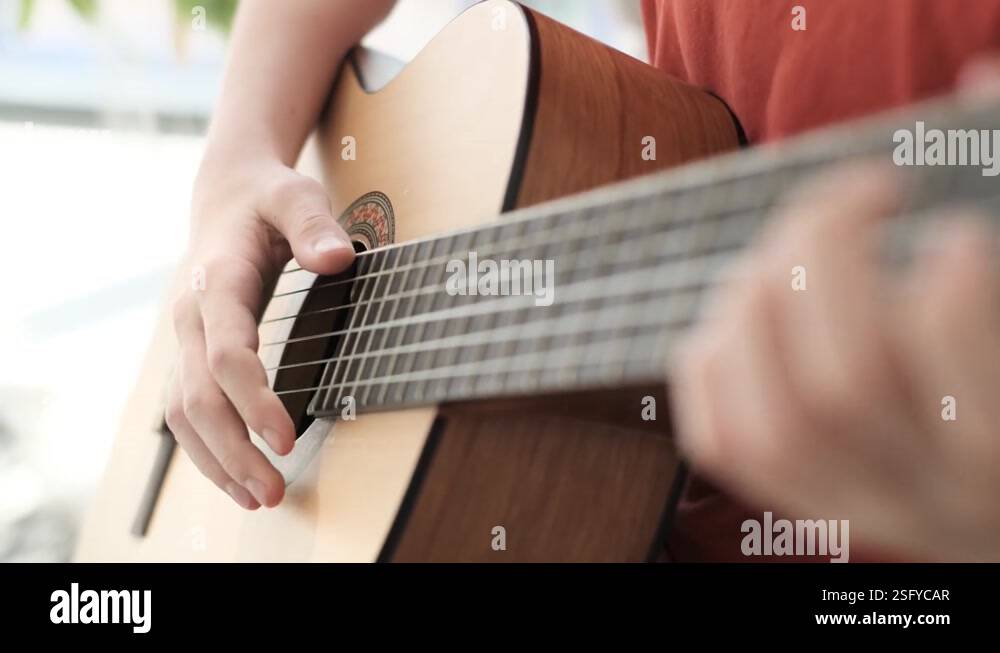 A teenage boy plays the guitar. A hand plays on the strings of a guitar ...