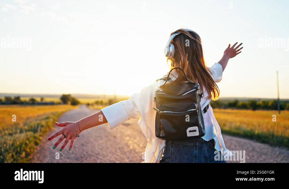 Teenage girl running across field wearing headphones and waving her ...