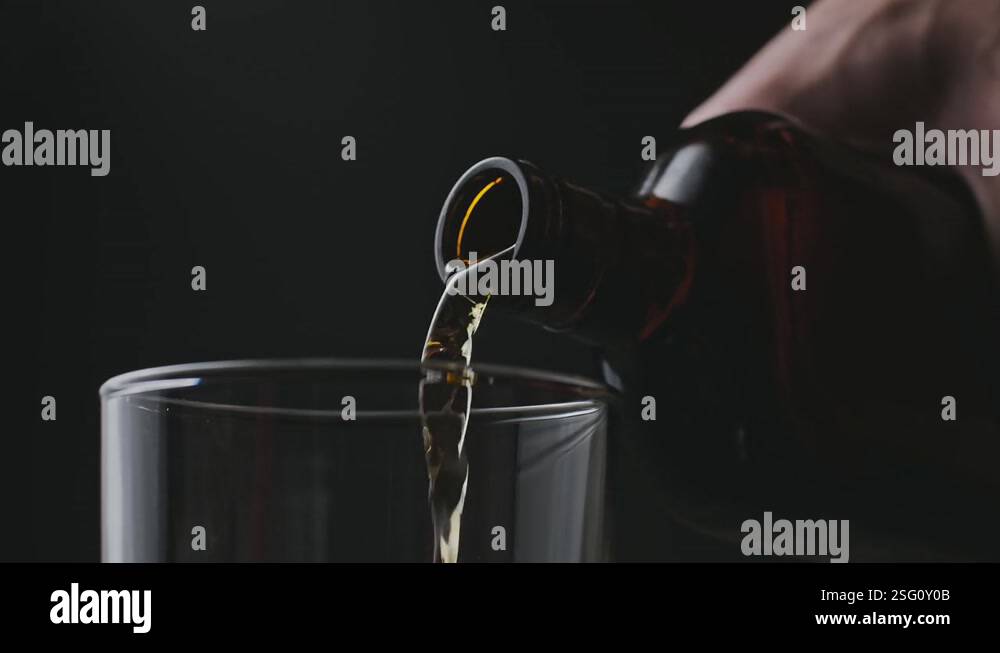 Whiskey poured in glass from brown bottle at black background. Pouring ...