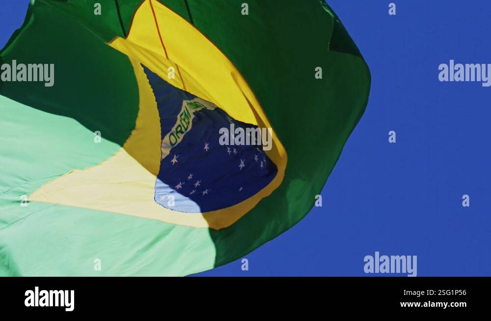 The Brazilian flag waving in the wind in slow motion with a blue sky ...