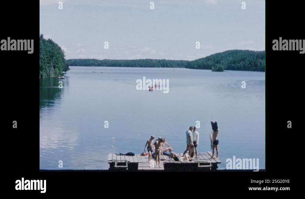 1960s: Camp. Path through woods. Men and boys on dock. Canoes on pier ...
